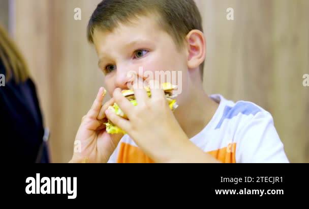 Cute boy eating large hamburger at fast food restaurant. Unhealthy meal ...