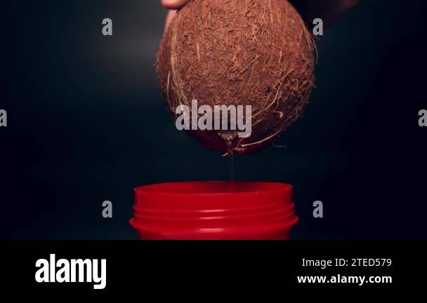 Splashing of coconut water. Pouring liquid to the red cup. Front view ...