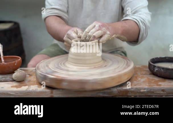 A rotating potters wheel and pottery on it, taken from the side. a man ...