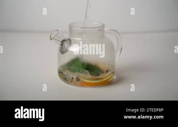 Pouring boiling water into the teapot with lemon, orange, mint leaves ...