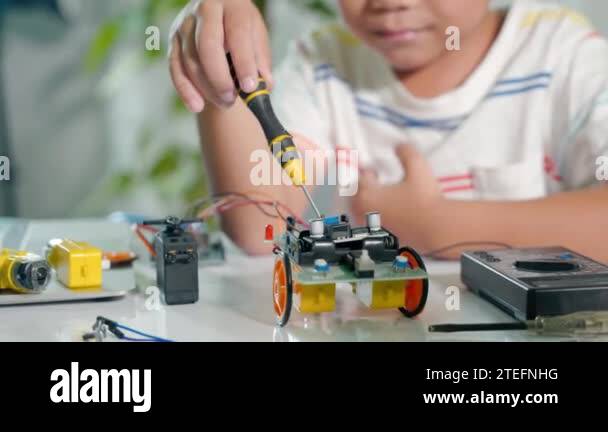 Asian kid boy assembling the Arduino robot car homework project at home, Little child tighten ...