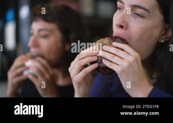 Two people eating burgers. Young women taking a bite of cheeseburgers ...