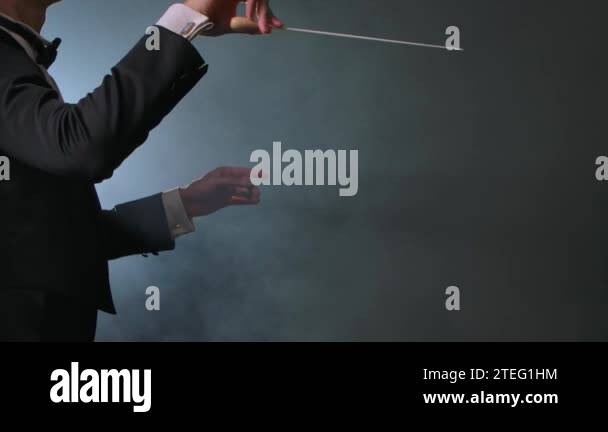 Side view of man gracefully waves conducting baton to synchronize and ...