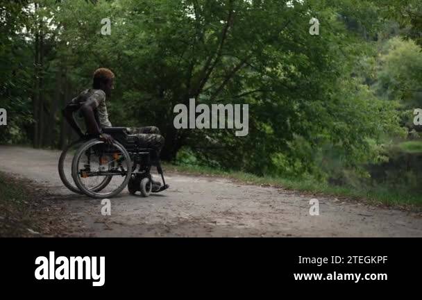 Wide shot African American soldier in wheelchair rolling to lake shore ...