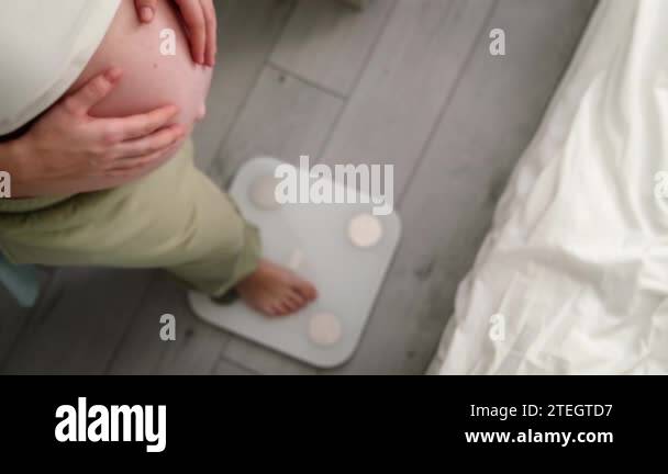 Young woman measuring her pregnant weight standing on scales ...