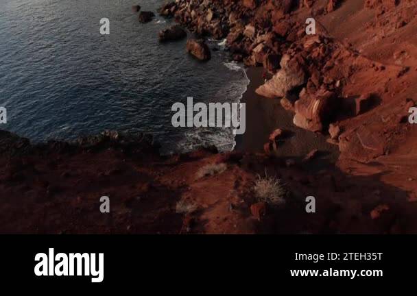 Aerial dolly tilt up over small bright red rusty sand beach with ...