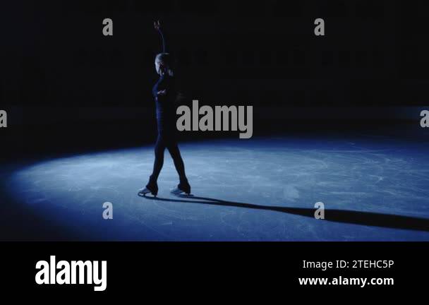 Woman appears on ice arena in blue light of spotlight and slides over ...