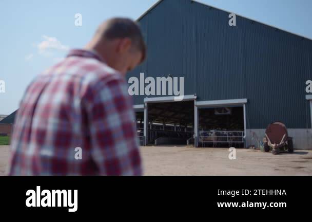 Farm worker sitting outside big barn facility on farmland ranch close ...