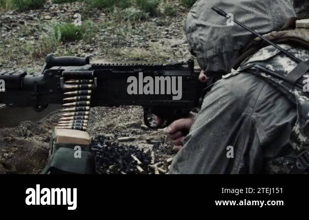 Shot of a soldier firing a belt-fed machine gun from a sitting position ...