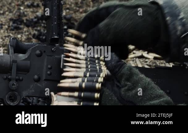 Close-up of gloved hands loading a chain of rounds into the feed tray ...