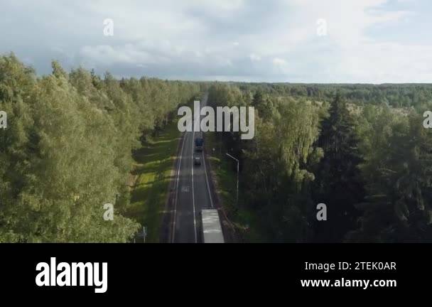 A busy highway surrounded by trees along which trucks and cars drive ...