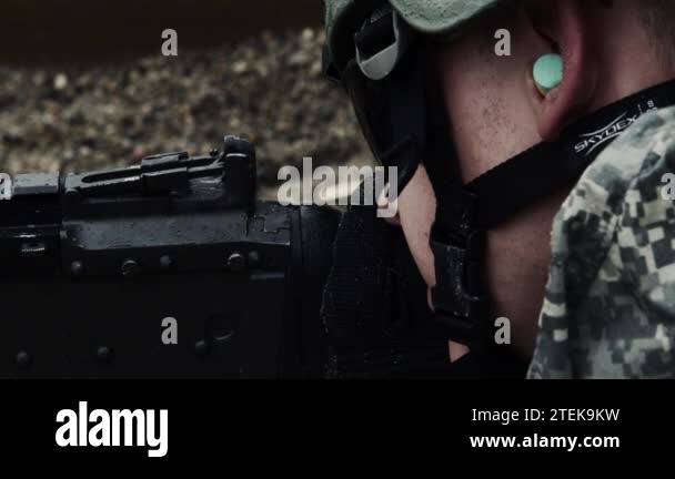 Close-up of a soldier aiming a belt-fed machine gun and firing. He is ...