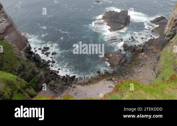 A slow tilting shot, rising from a rocky bay to reveal waves crashing ...