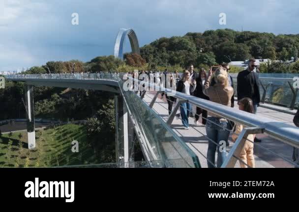 Crowd of people walking by pedestrian glass bridge with a bicycle path ...