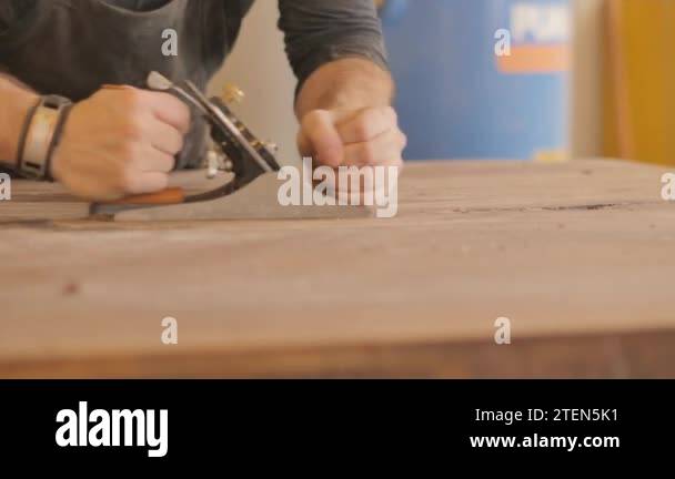 An experienced artisan carpenter is hand planing a natural wood table ...