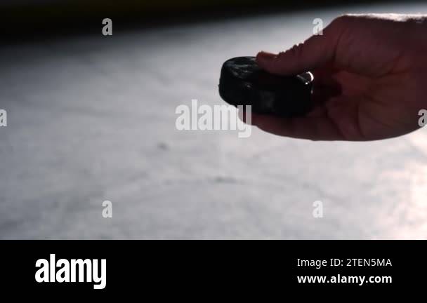 A mans hand throws black hockey puck on ice of the arena to start the ...