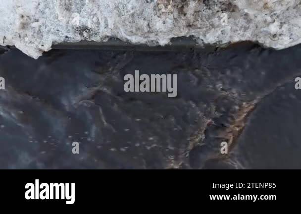 Puddle. Dirty water melted from snow flows along curb of road after ...
