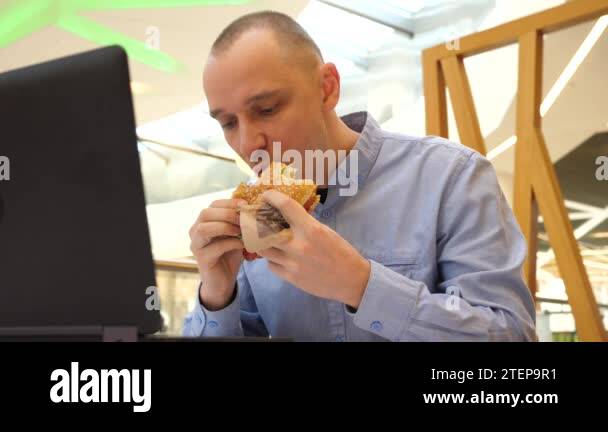Young man working remotely from a city mall food court eating big tasty ...