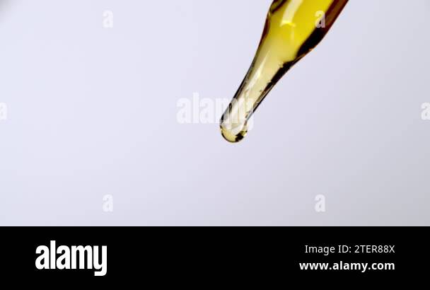 Yellow liquid drops falling from glass pipette, close up view isolated ...