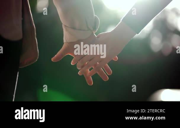 Two people joining hands outside with sun flare in background. Closeup ...