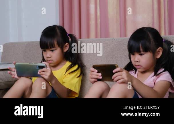Two Sisters Are Playing Online Games On Their Smartphones Sitting On