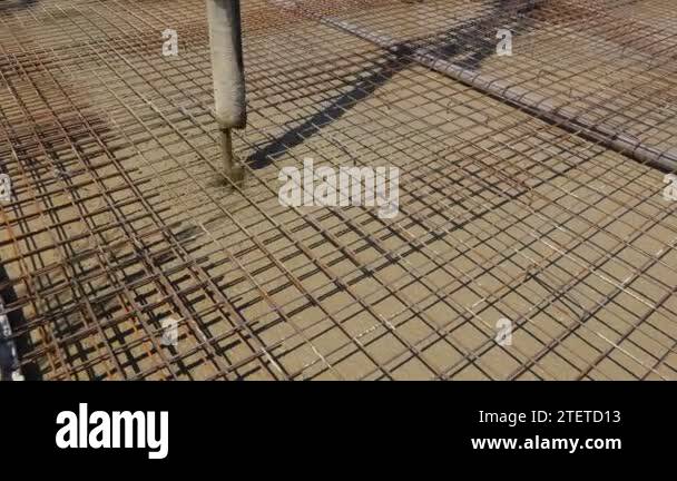 Pump hose is pouring fresh concrete over square reinforcement in the ...