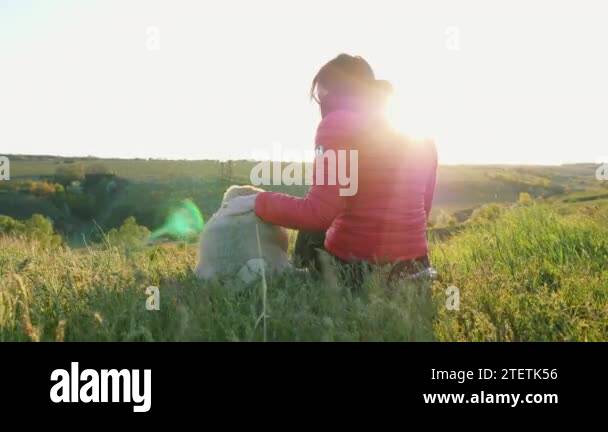 Woman hugs her dog on sunset. Pug and woman sit in nature and rest on ...