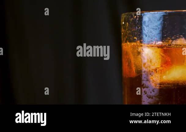 Luxury whiskey. Ice cubes fall with splashes into a glass with golden whisky on the black ...