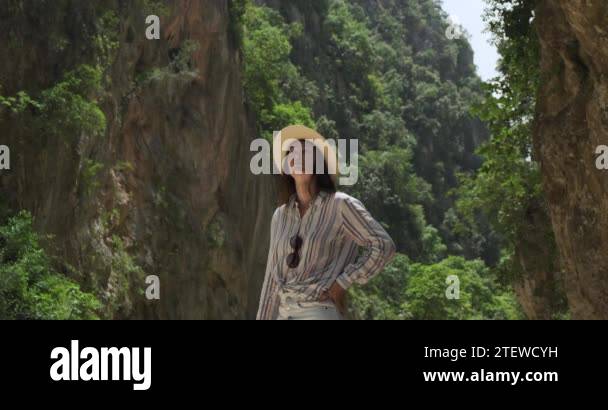 Medium shot, a girl in a hat looks around in a gorge with green trees ...