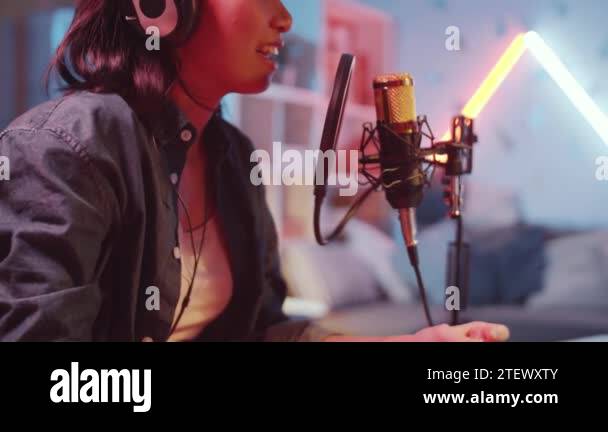 Close up view of young Asian female singer in headphones singing into ...