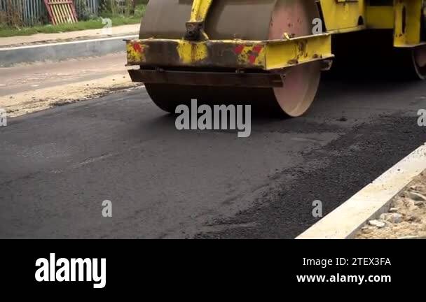 Compactor is driving over freshly poured asphalt and compresses it on ...