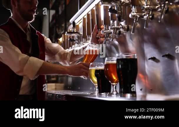 Bartender pouring beer into glasses at pub in neon light. Close-up view of barmans hand filling ...