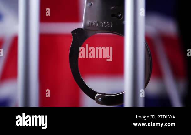 Handcuffs swing on prison bars with Union jack British flag background ...