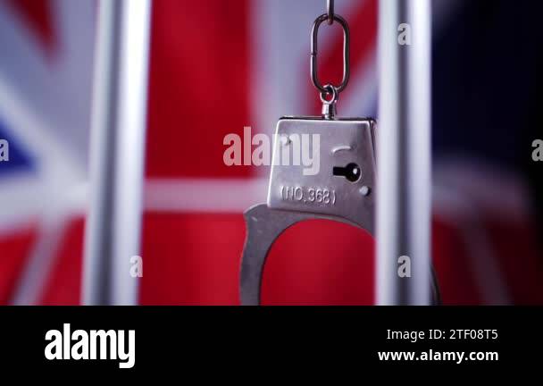 Handcuffs swing on prison bars with Union jack British flag background ...
