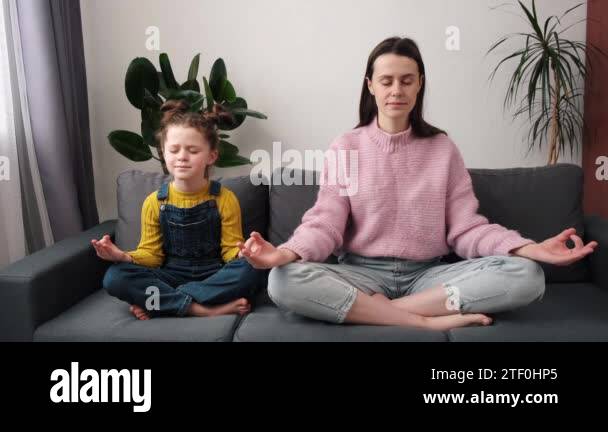 Healthy calm young mother with cute little daughter meditating with closed eyes while sitting in ...