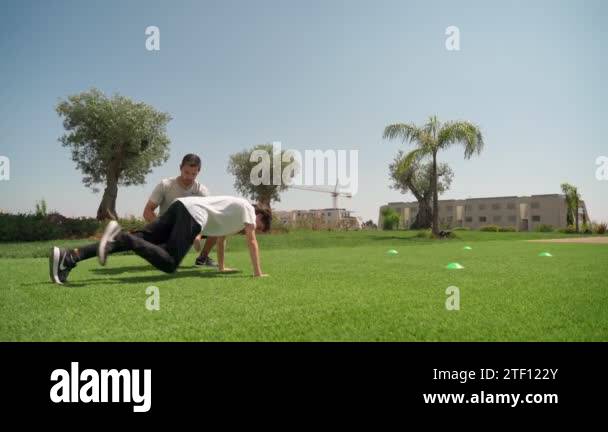 A young guy with a personal fitness trainer performs push-ups and ...