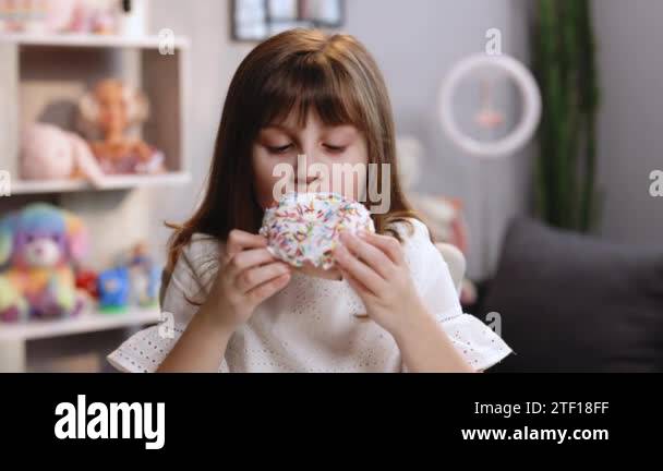 Child girl who is eating donut with colorful frosting and smiling ...
