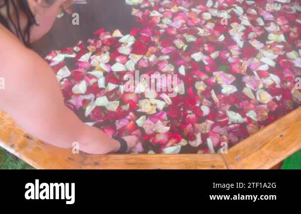 Beautiful young woman lying in a hot ofuro bath full of rose flowers ...