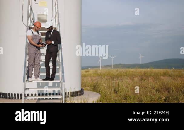 Multiracial partners standing on stairs near wind turbine and looking ...