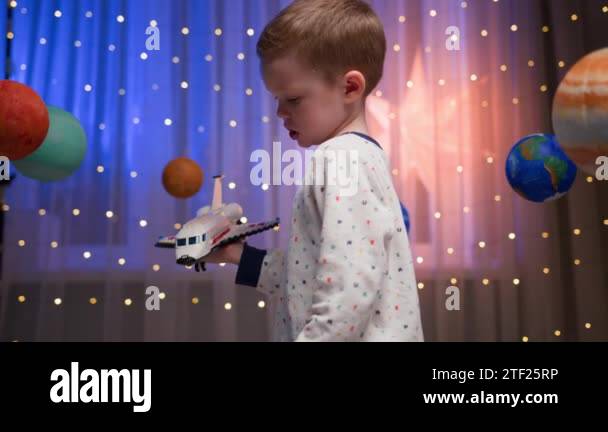 Portrait boy is playing with toy space shuttle, flying in space among ...