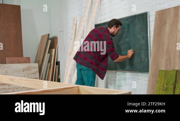Young carpenter build a solid wood wall in a carpentry workshop A joiner draws a design of a ...