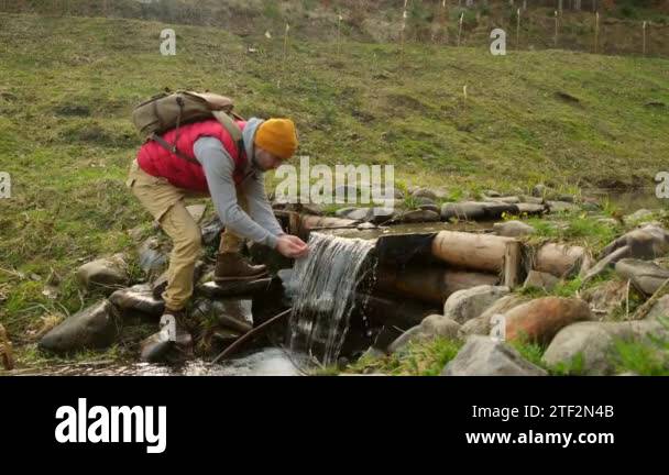 man drinking water from stream with her hands. male hands draw water ...
