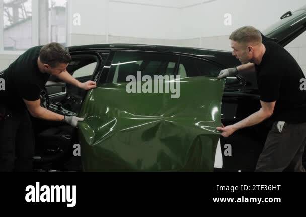 Two men are vinyl wrapping a car in dark green color, applying wrap to ...