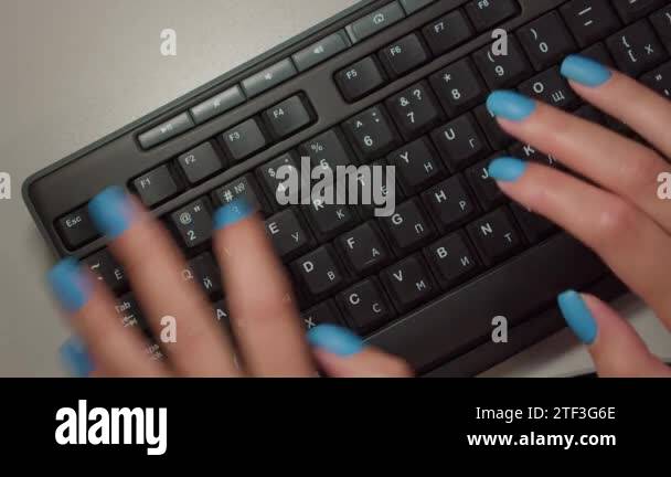 Woman with blue nails types on computer keyboard at table upper close ...