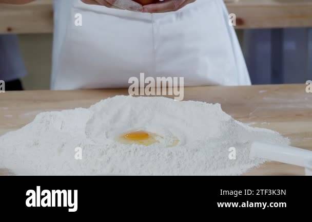 Baker break eggs to the flour lying on the wooden cooking table. Slow motion Stock Video Footage ...