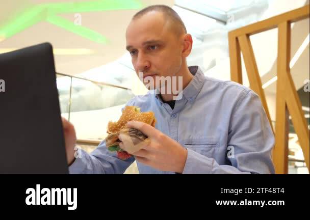Young man working remotely from a city mall food court eating big tasty ...