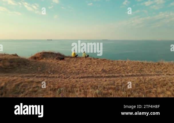 Two travelers with dog sitting on the edge of cliff and overlooking the ...