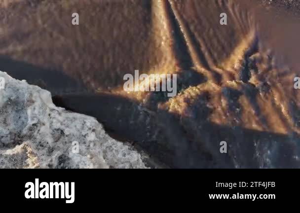 Puddle. Dirty water melted from snow flows along curb of road after ...