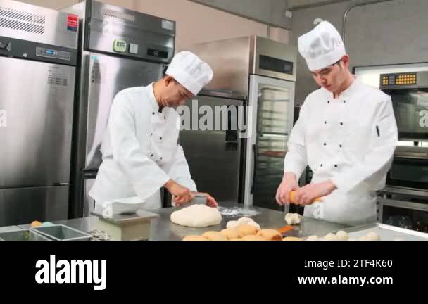 Two professional Asian male chefs in white cook uniforms and aprons are ...