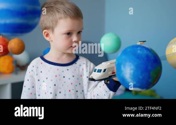 Portrait boy is playing with toy space shuttle, flying in space among ...